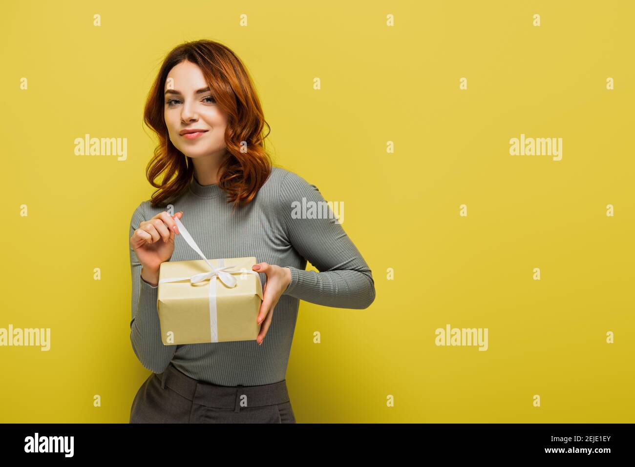 happy young woman pulling ribbon on present and smiling on yellow Stock ...