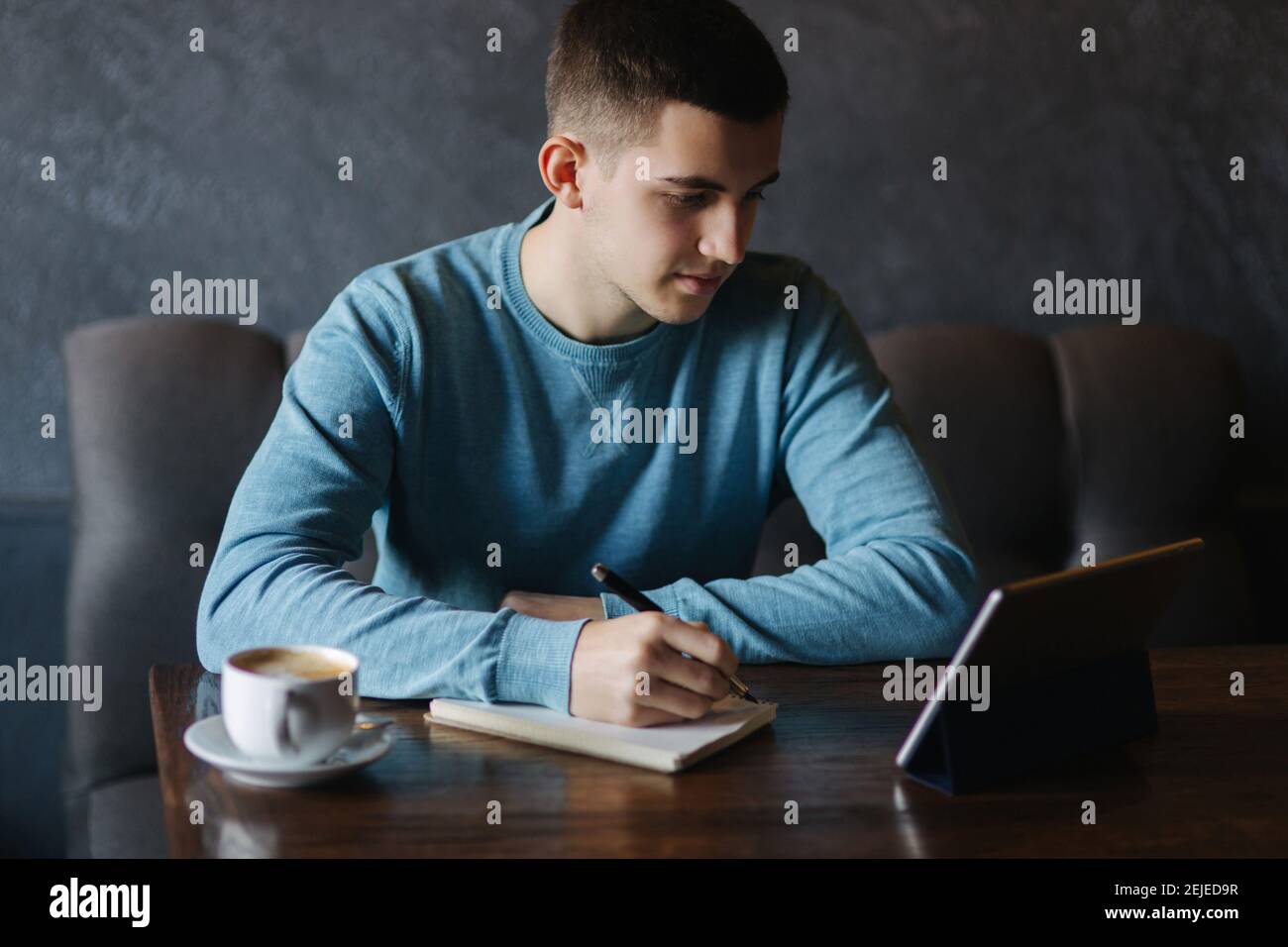 Man is sitting in a cafe and uses a tablet and write down something in ...