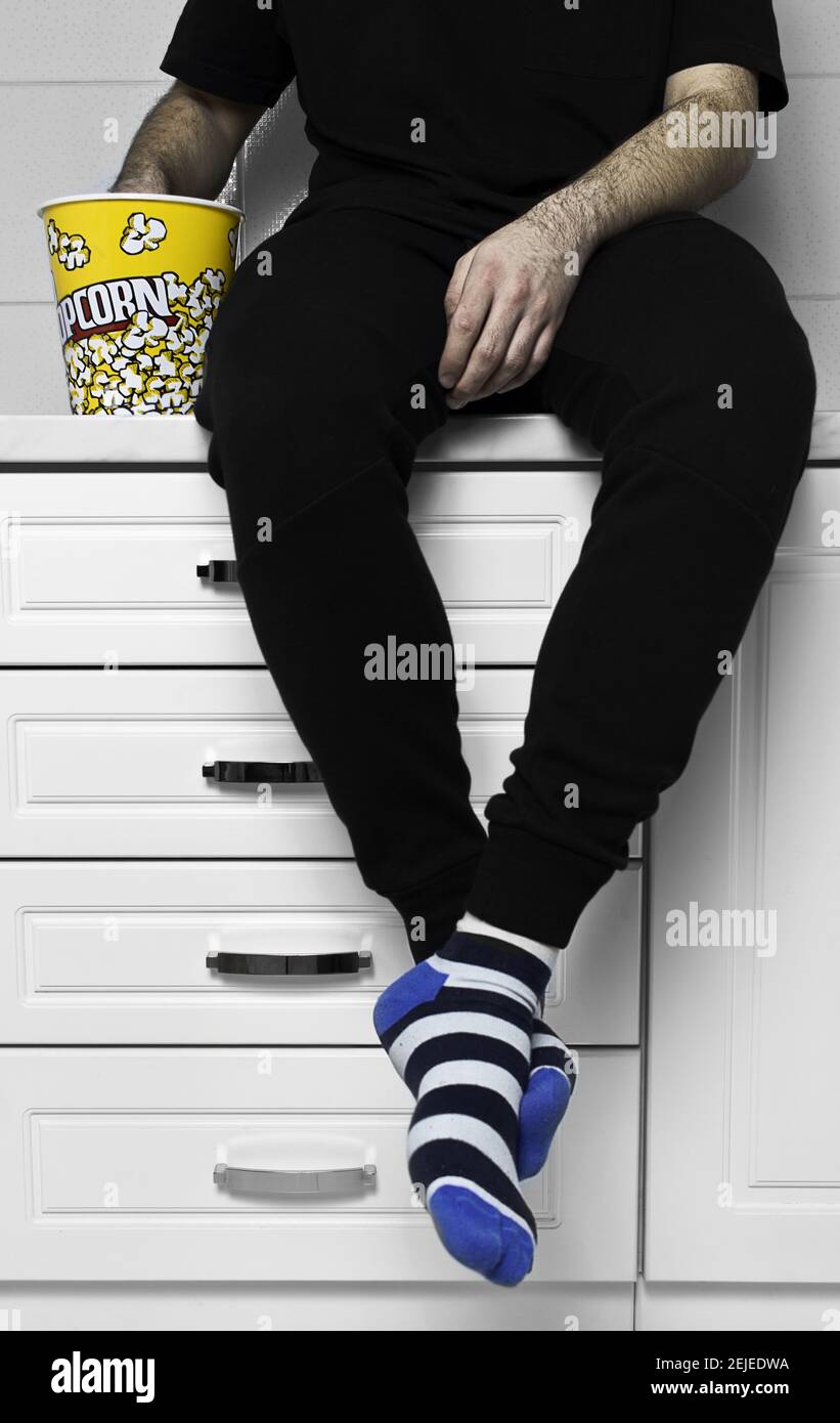 Vertical hot of a man with colorful socks sitting on a drawer eating ...