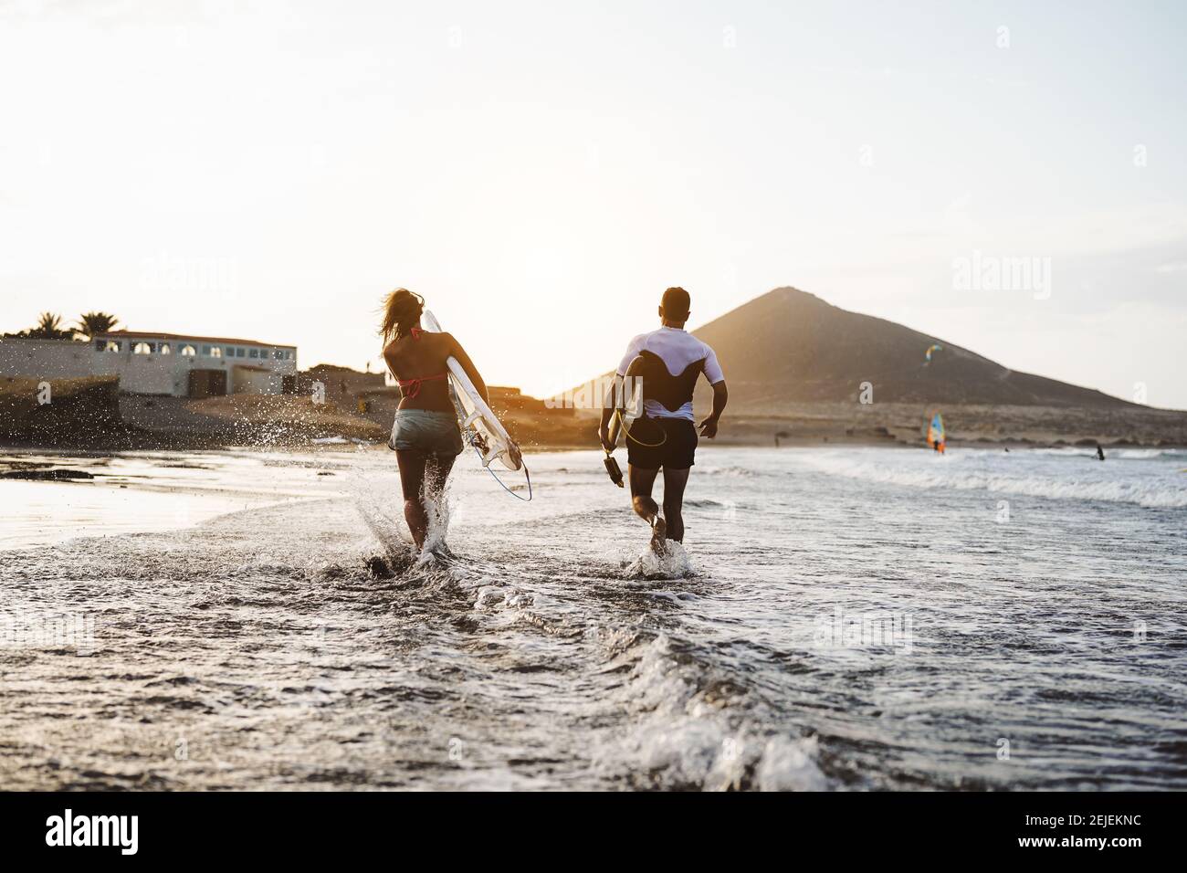 Happy surfers running in the water at sunset time - Young couple having ...