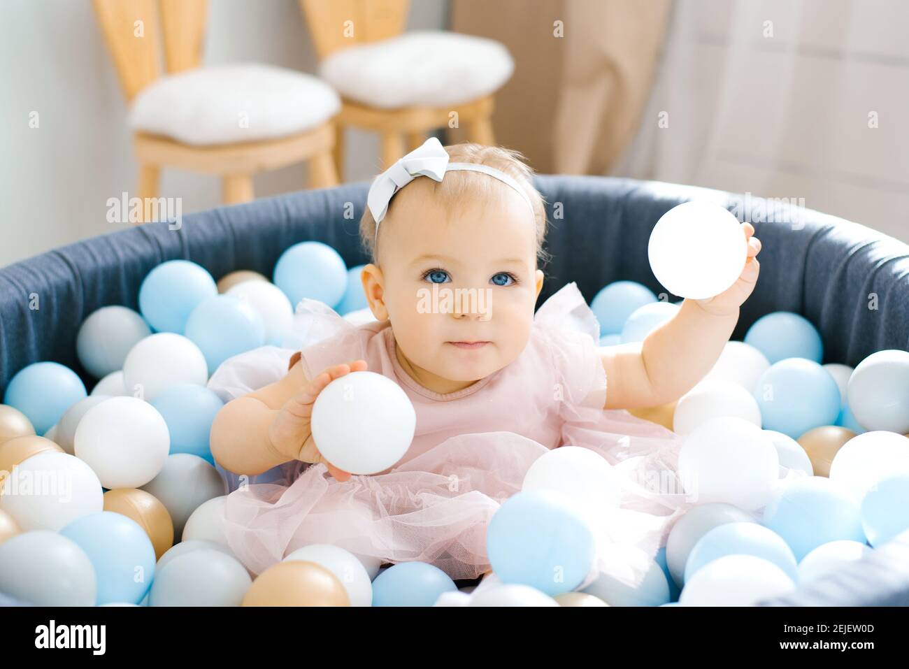 A cute blue-eyed one-year-old baby in a pink dress is bathing in a toy ...
