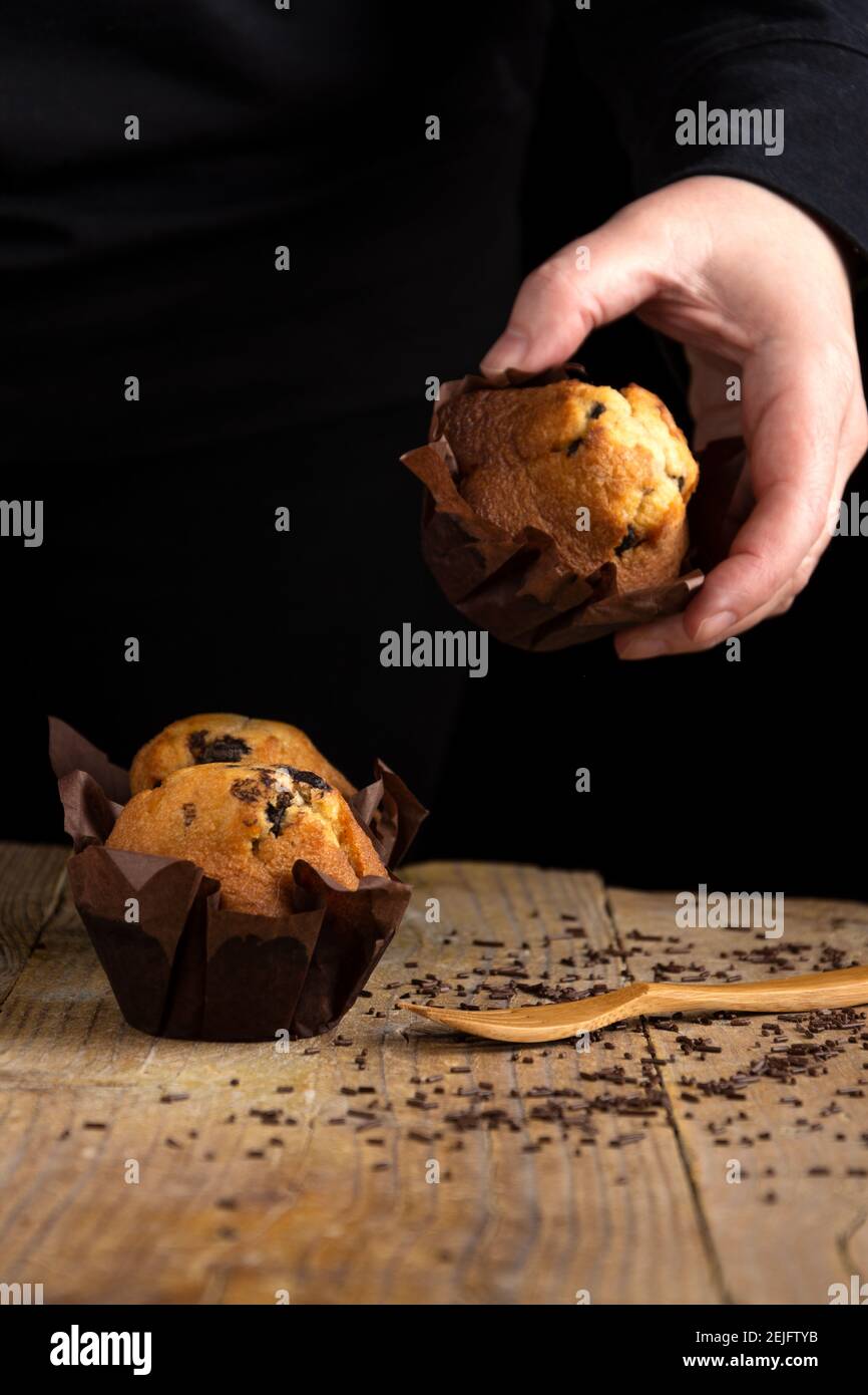 View of woman's hand holding a muffin, on wooden table with two ...