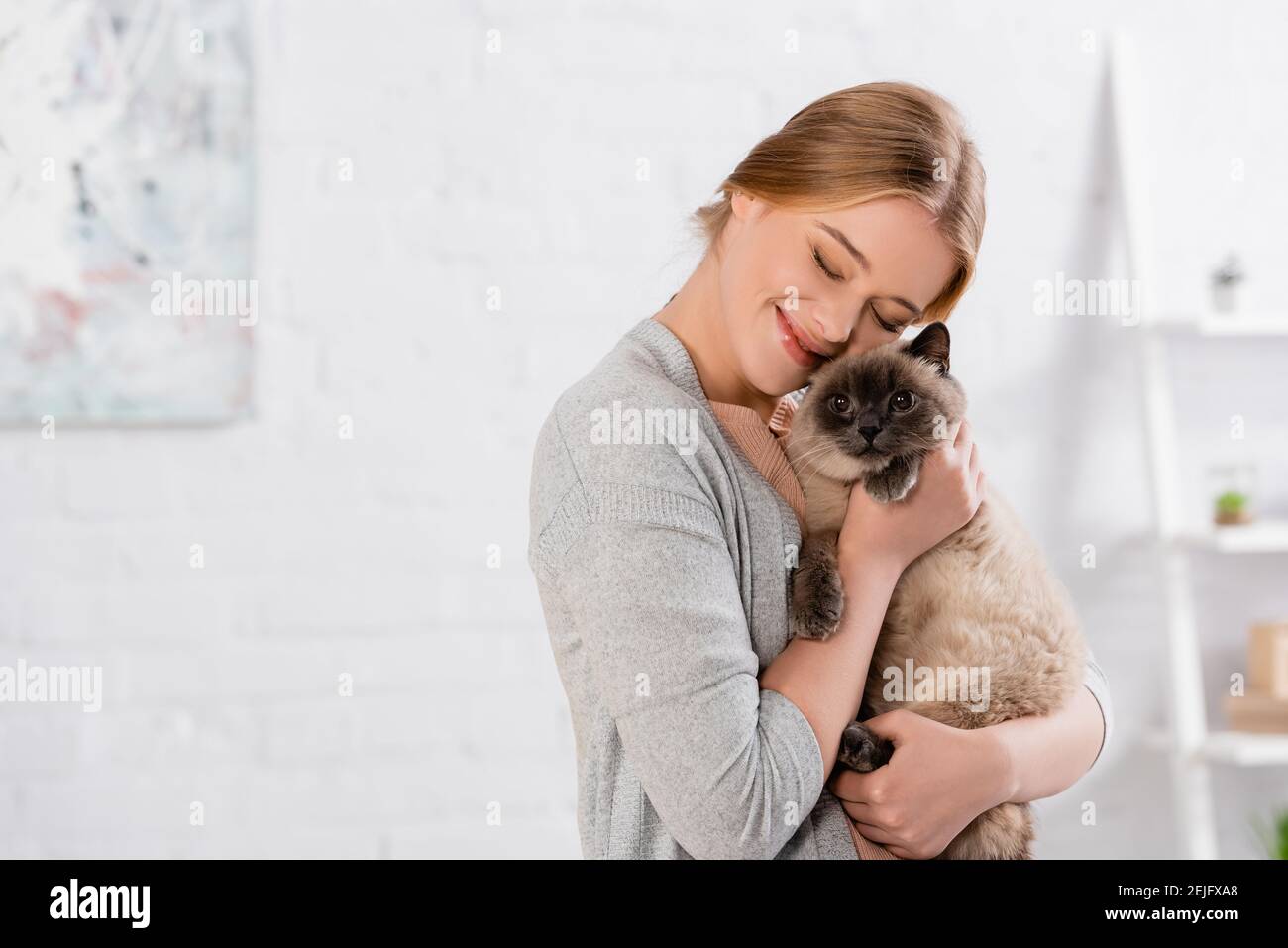 Smiling woman with closed eyes embracing siamese cat Stock Photo - Alamy