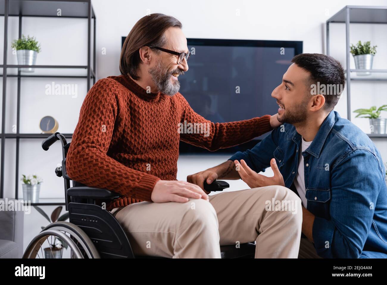 happy disabled man touching shoulder of excited hispanic son talking to ...