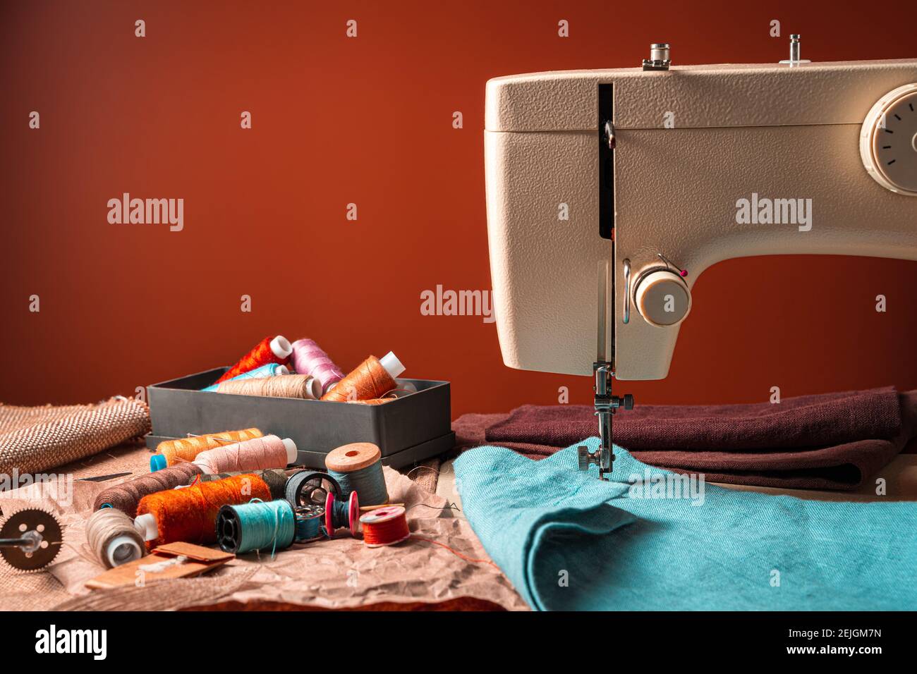 Colored threads, fabrics, and a sewing machine on a brown background ...
