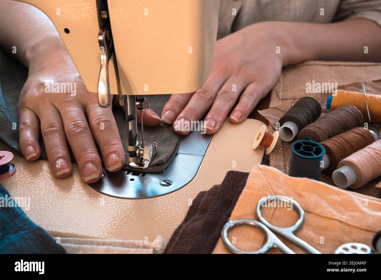 Women's hands sew on a sewing machine against the background of fabrics ...