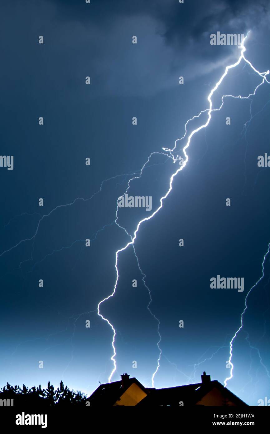 Vertical shot of lightning in the night sky over the village houses ...