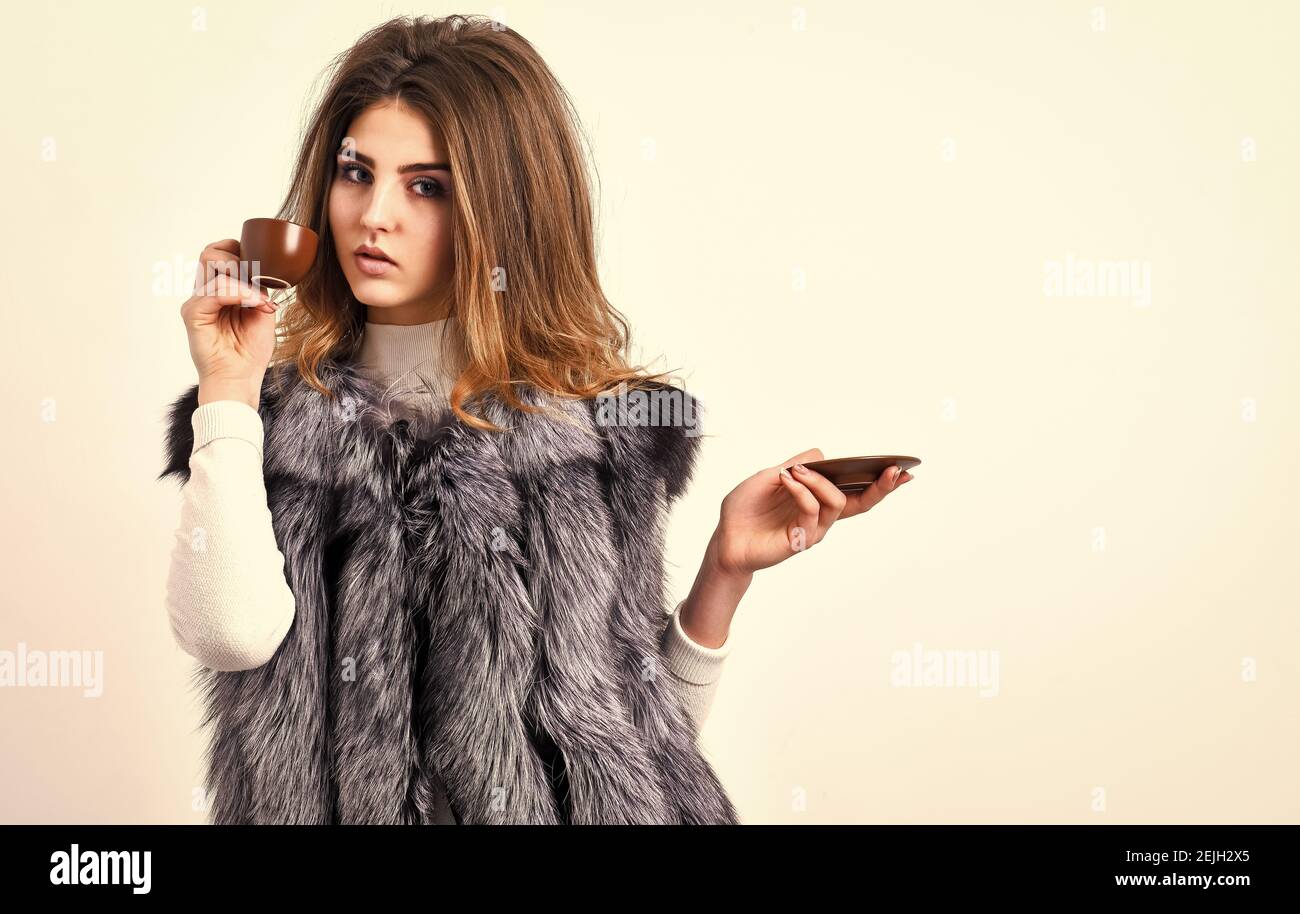 Woman splendid makeup wearing luxurious fur coat drinking hot coffee ...