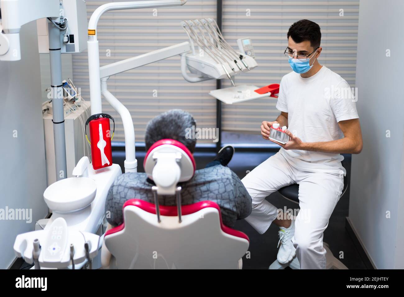 Dental surgeon with dental crown in hands model talks to patient about ...