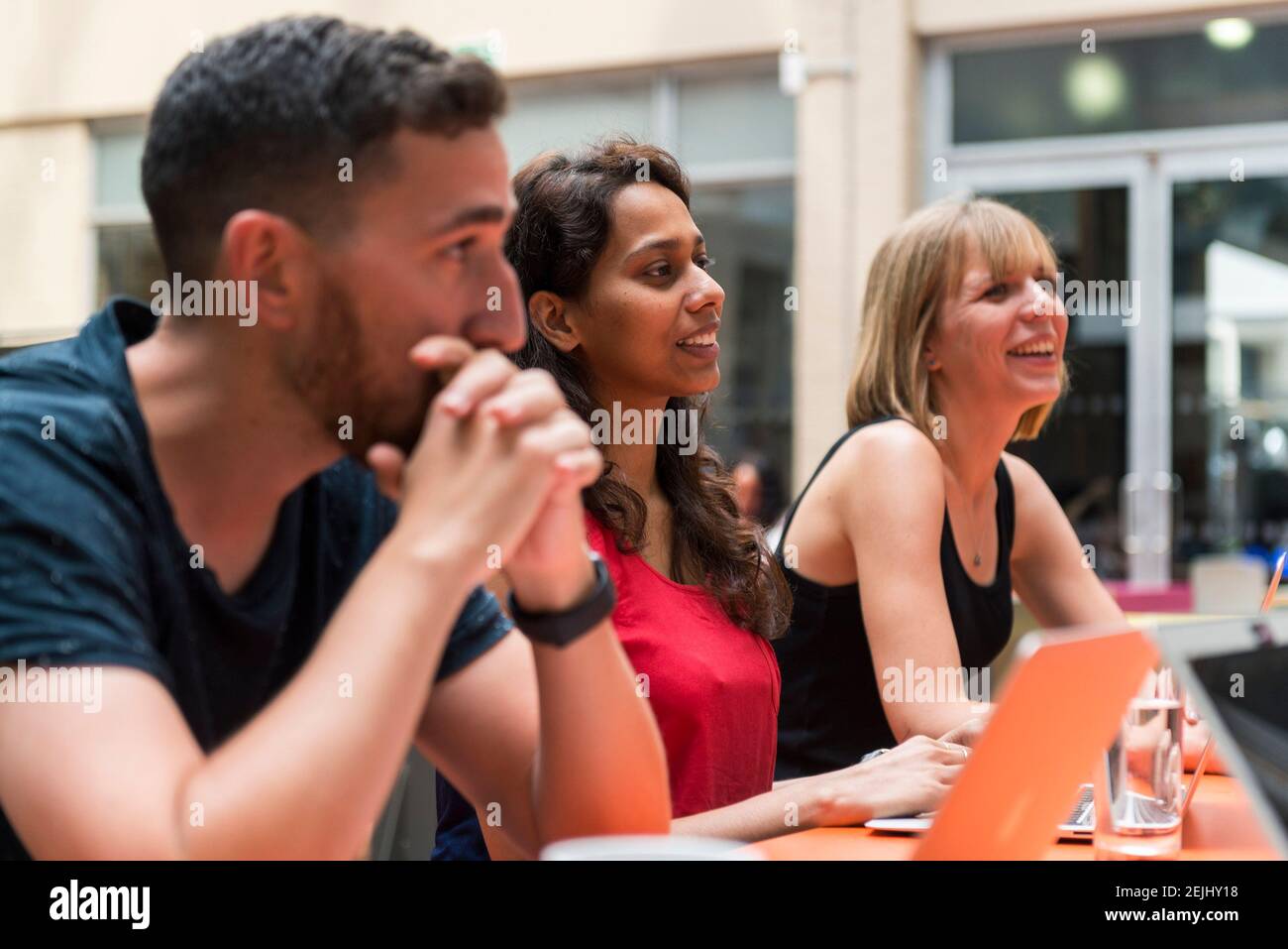 Six workers sit round an open plan meeting table in a communal space in ...