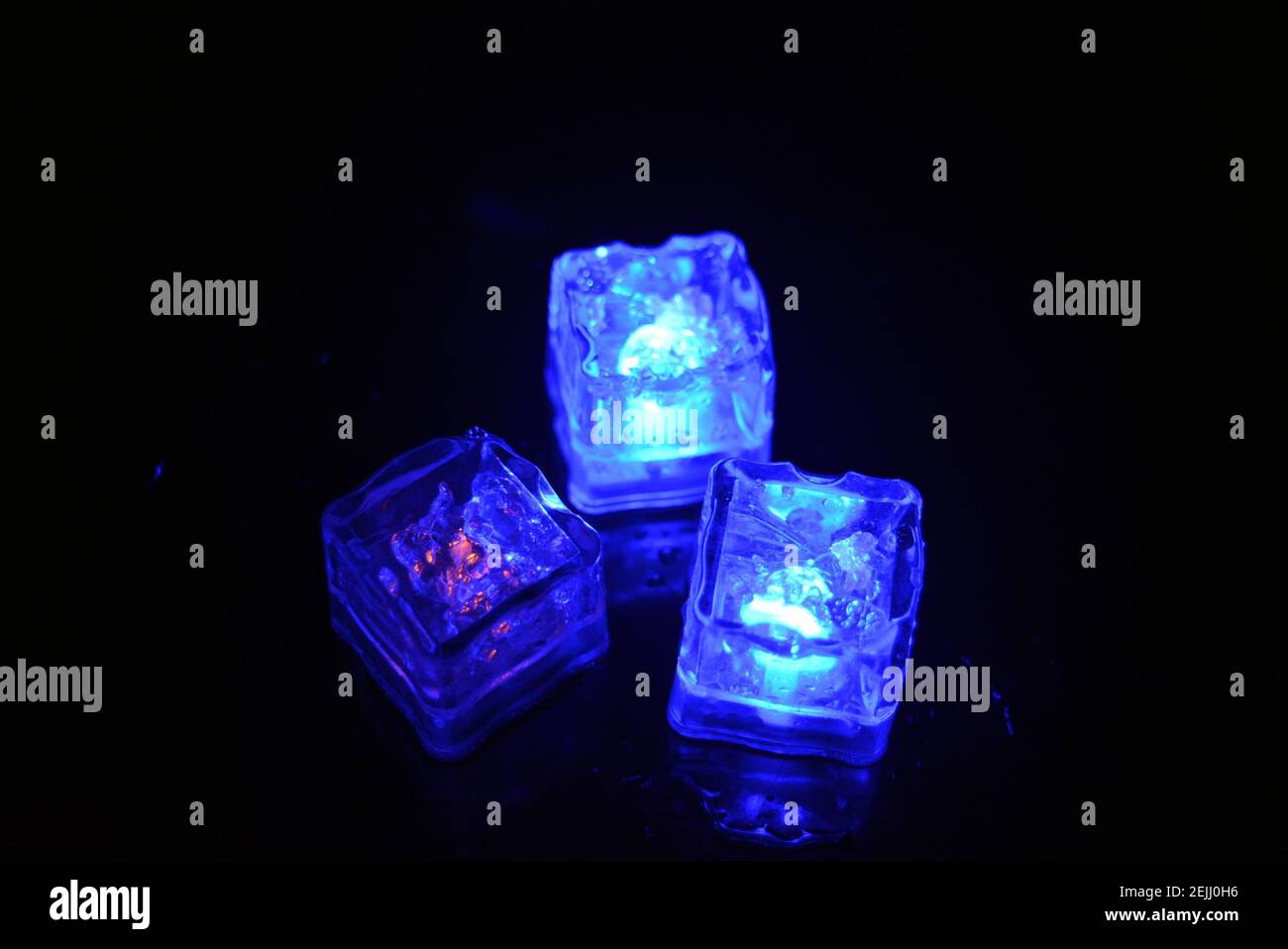 Multicolored, blue glowing ice cubes float in champagne glass that ...