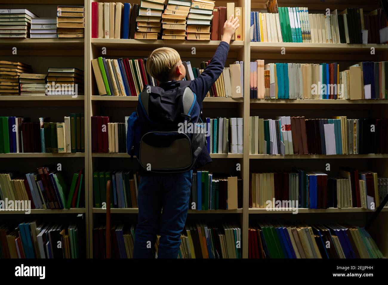 rear view on pupil boy in library, boy taking a book from multi colored ...
