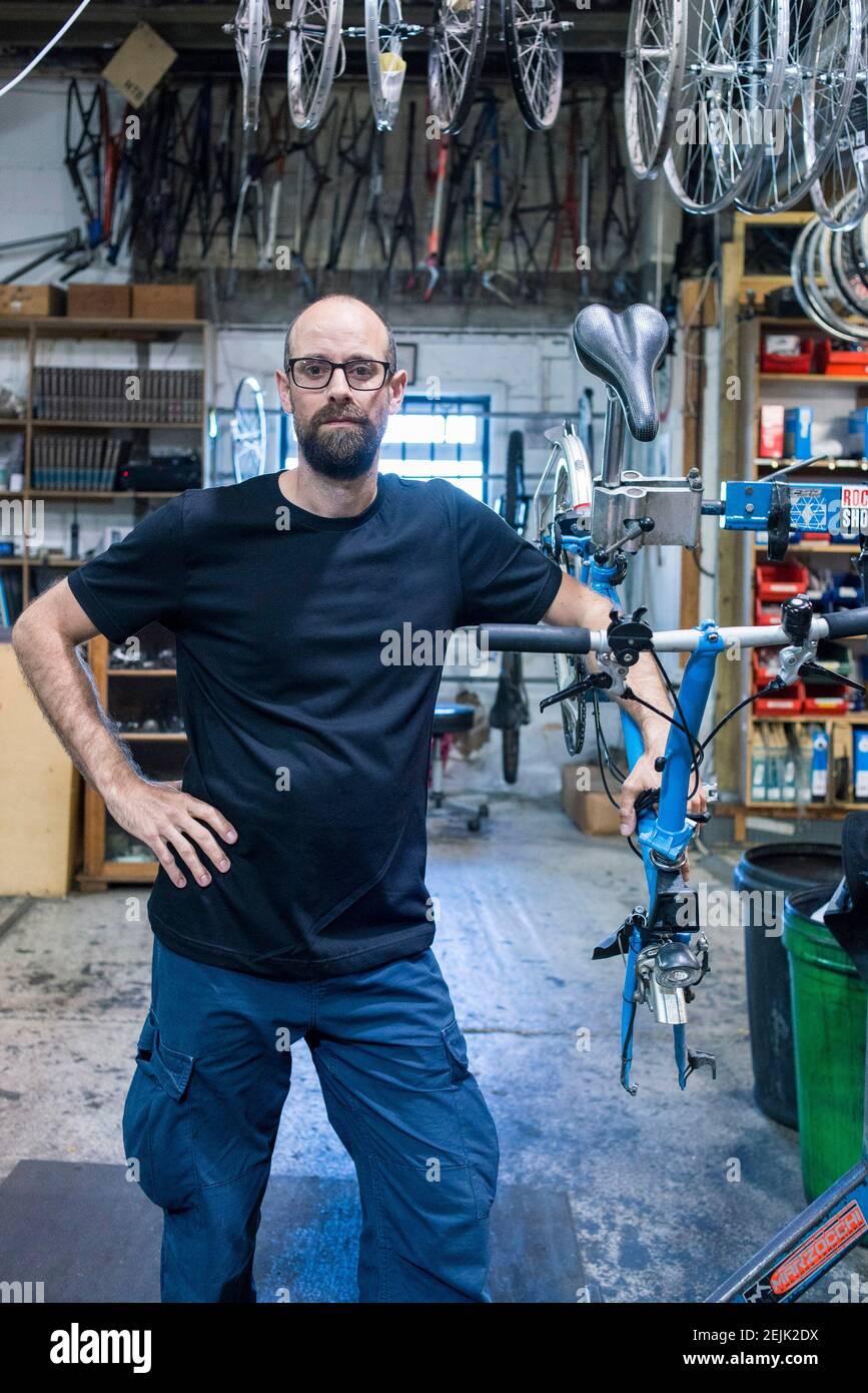 A bike technician stands at his work station and poses for a portrait ...