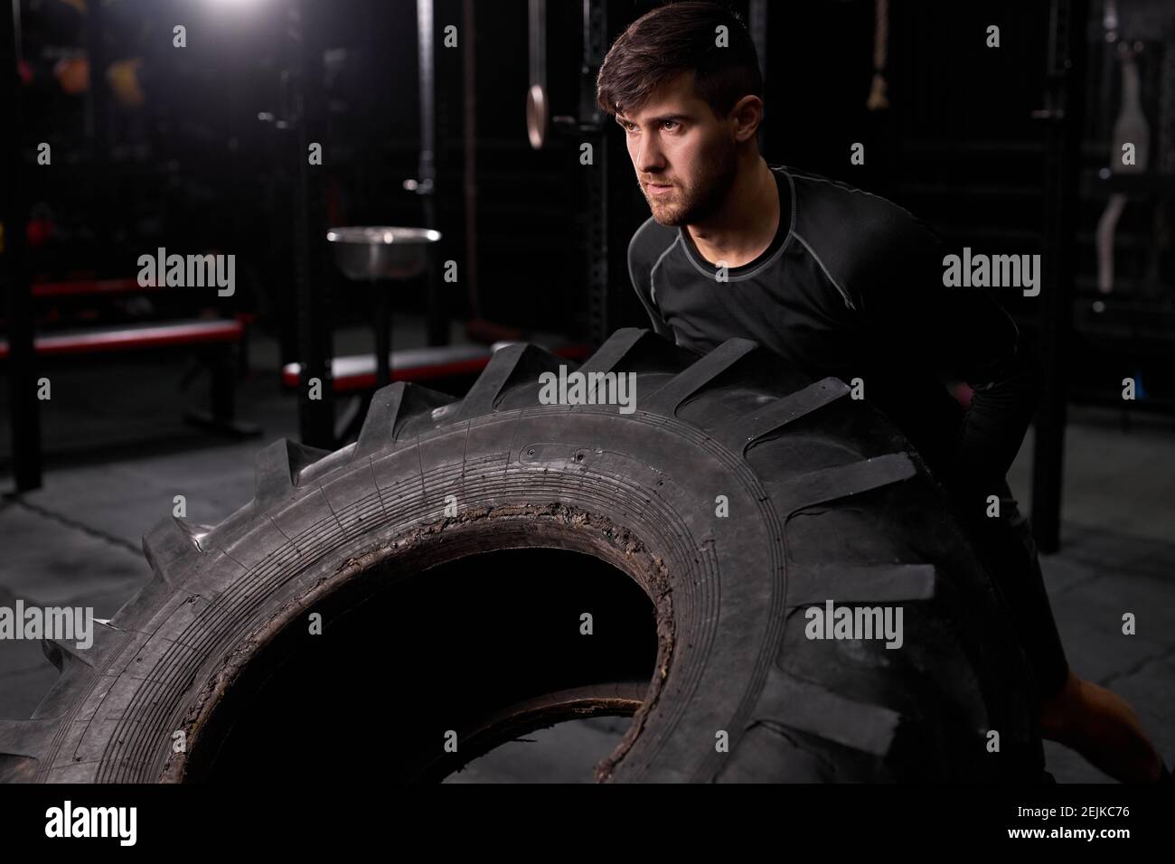 Fit male athlete doing tire-flip exercise indoors in modern gym. Cross ...