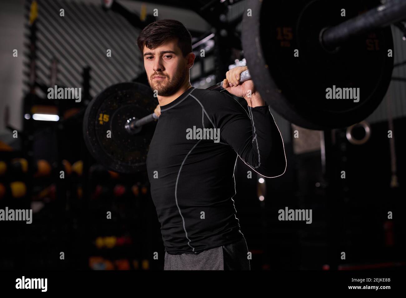 bodybuilder guy prepare to do exercises with barbell in dark modern ...