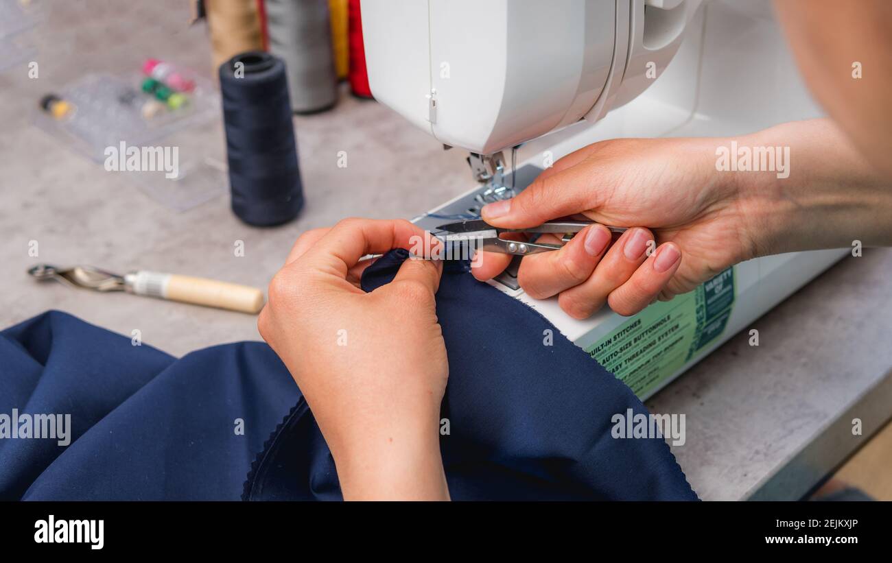 Cheerful woman sewing while sitting at her working place in fashion ...