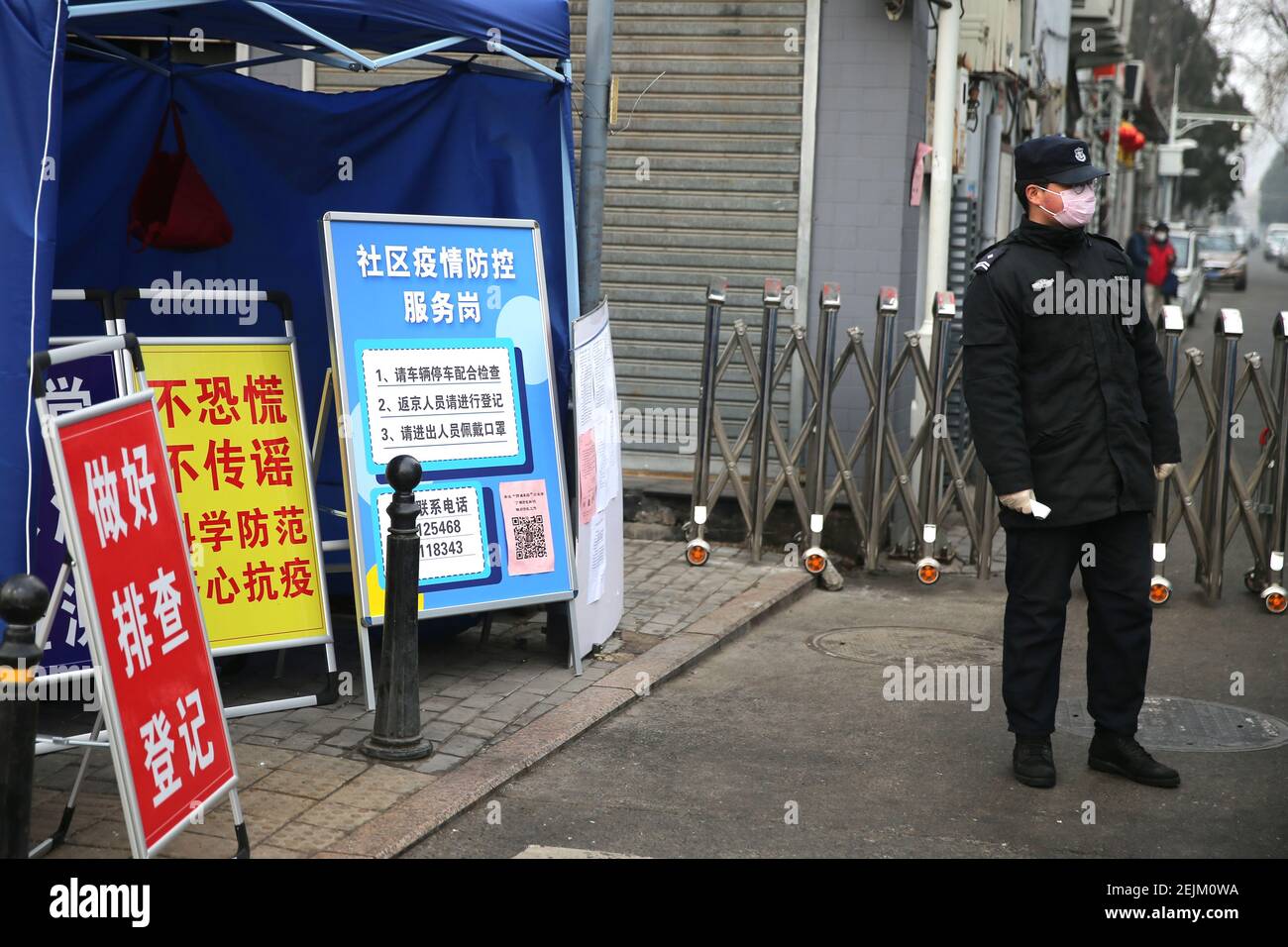 A masked Chinese security guard stands next to signboards with slogans ...