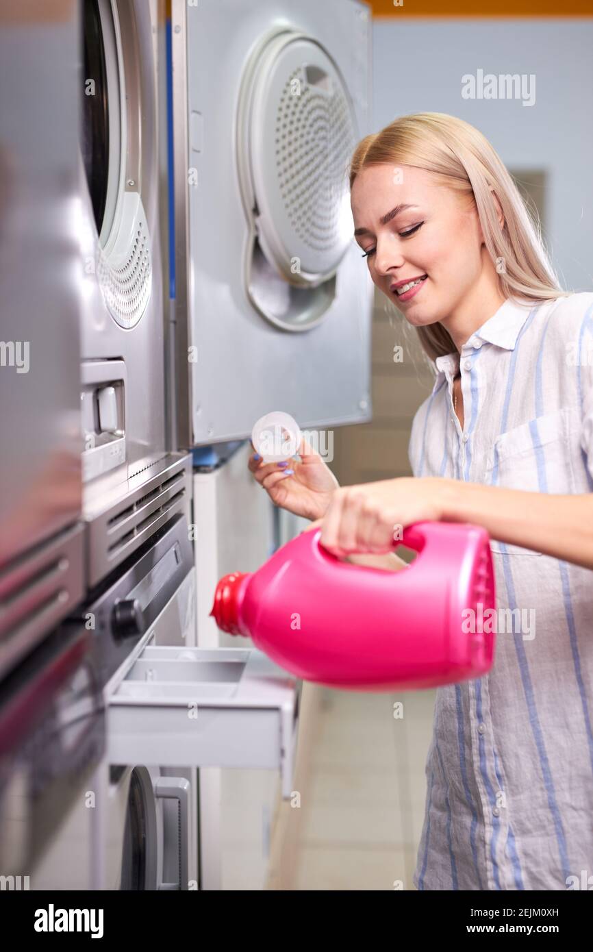 female pours a greasy detergent from pink bottle into the washing ...