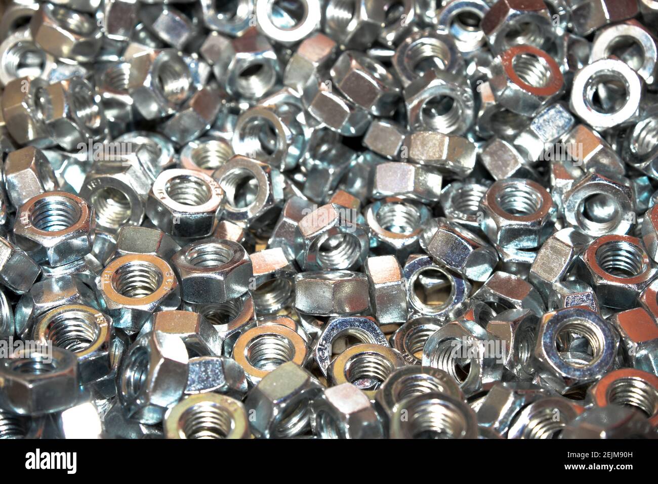 Lots of industrial galvanized steel nuts on a a big pile in warm light ...