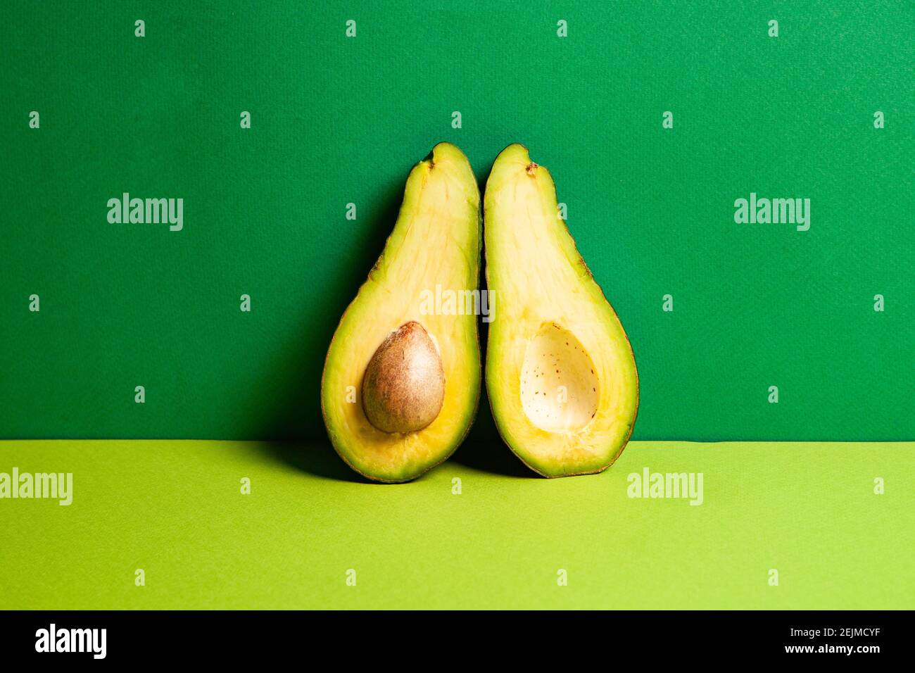 Whole ripe avocado near halved fruit against green background Stock ...