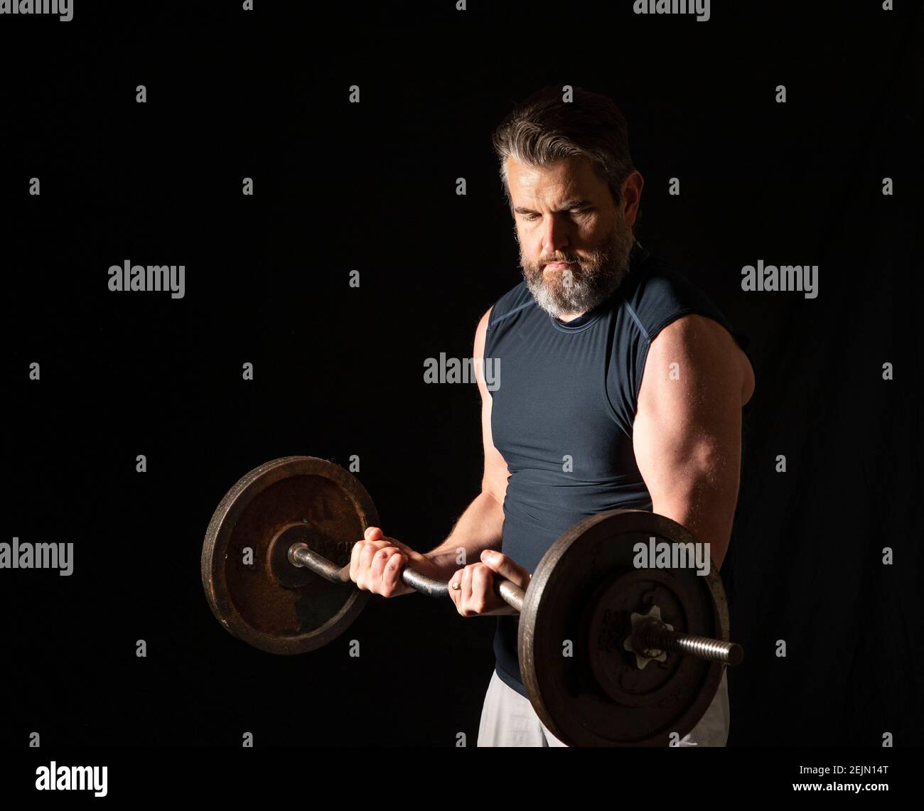 Strong, active, middle aged man with gray beard lifting heavy weights ...