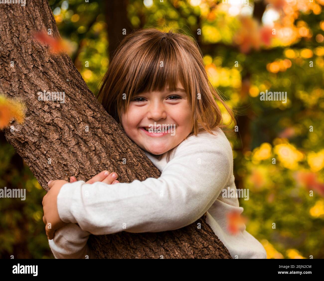 Little happy Girl hugging a tree with golden Autumn Foliage in the ...