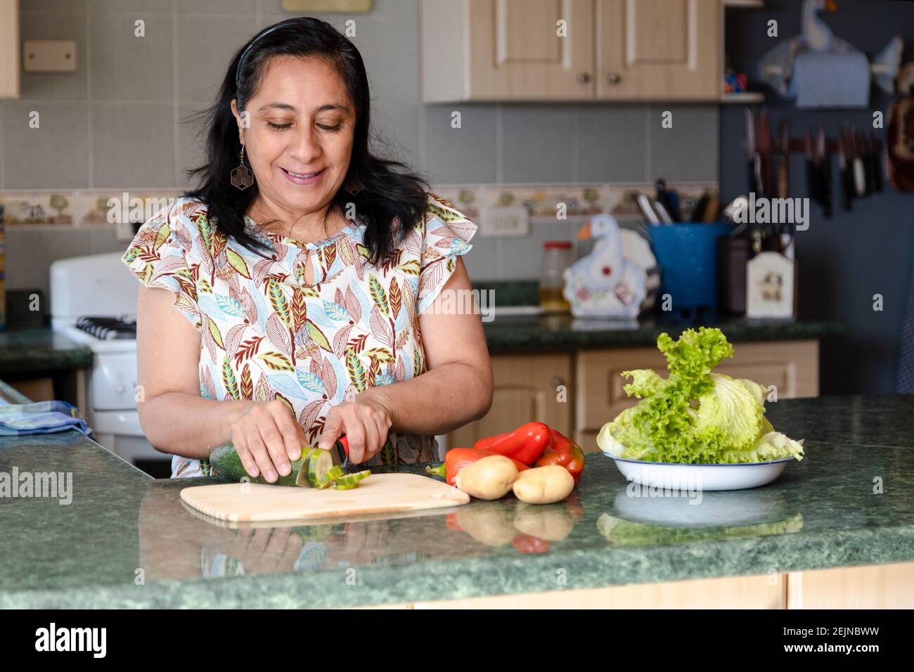 Smiling middle aged hispanic woman making fresh salad in her kitchen ...