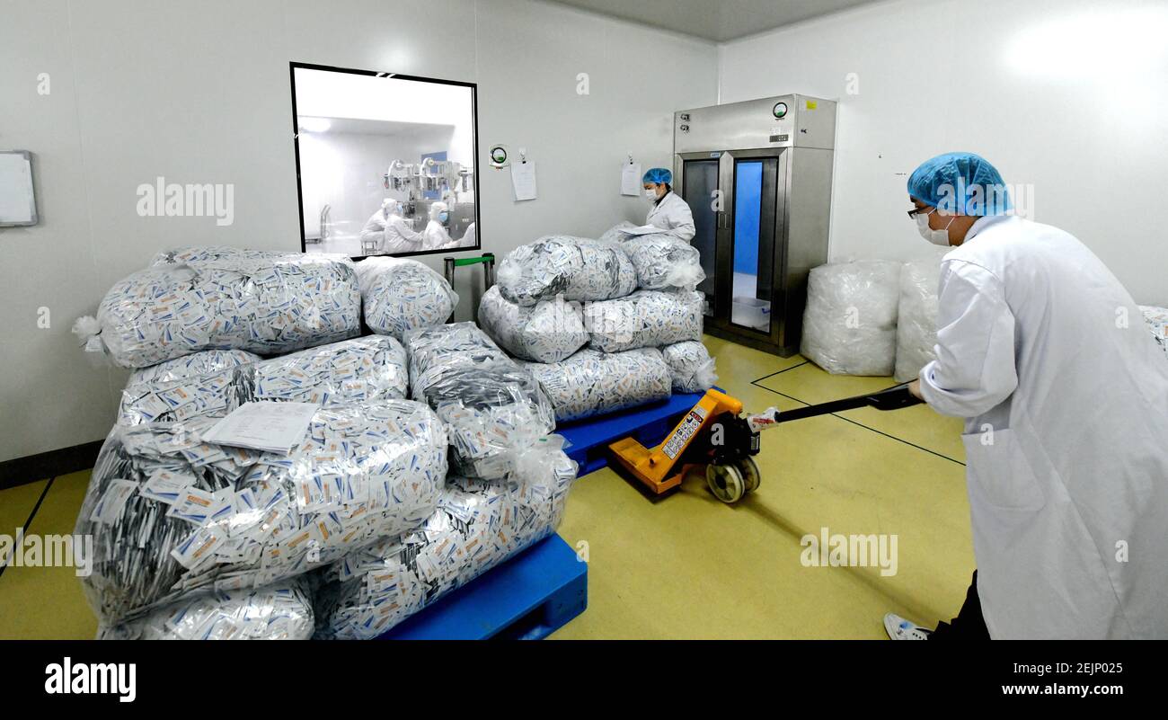 Staff with masks and protection suits work to produce medicine along ...