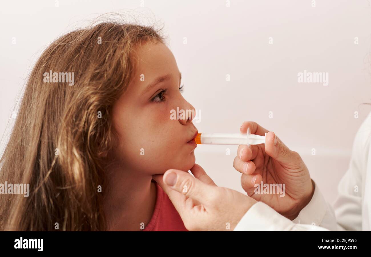 Female doctor giving syrup with syringe to a little girl at home. Home ...