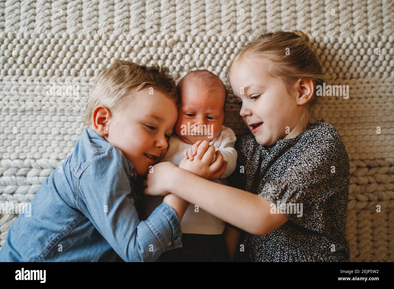 Beautiful white siblings lying on rug at home smiling holding hands ...