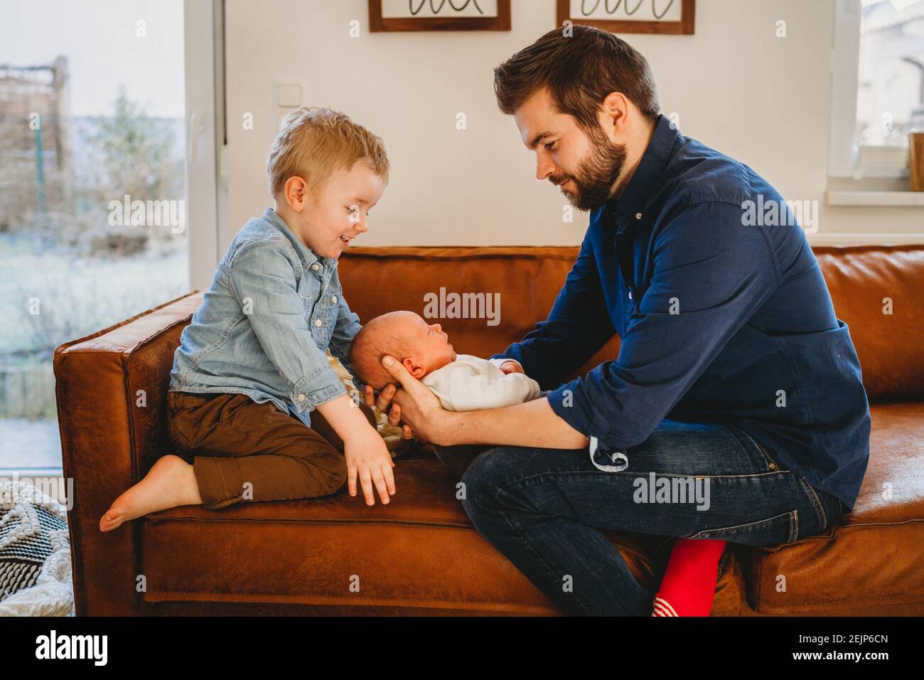 White dad and son smiling at newborn baby on sofa at home Stock Photo ...