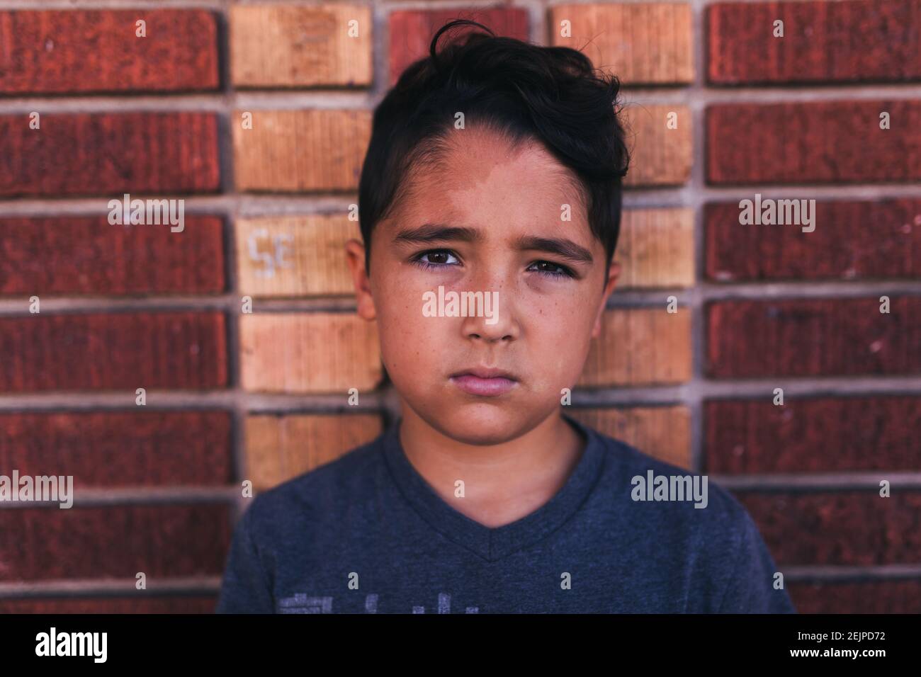 Boy standing in front of a brick wall looking mad Stock Photo - Alamy