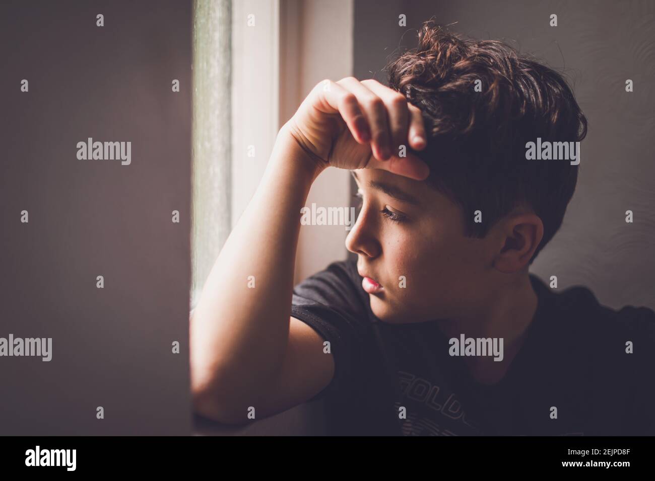Boy leaning against the wall looking outside a window Stock Photo - Alamy