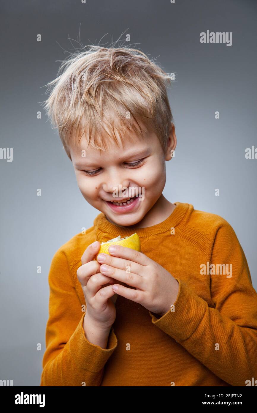 Happy child eating lemon in gray studio Stock Photo - Alamy