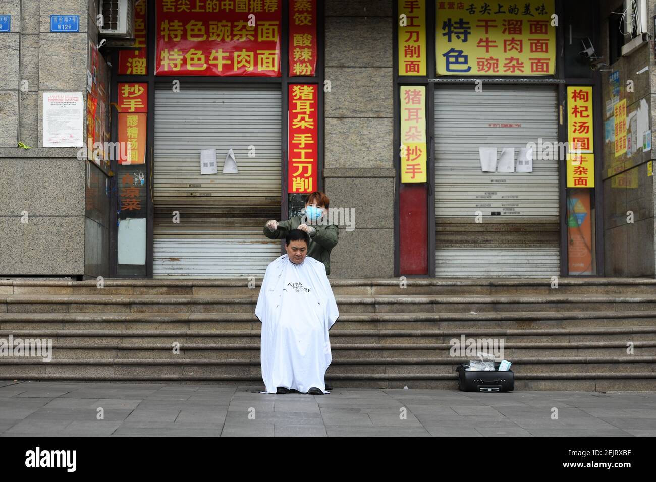 A barber does haircut for a person on the street in Yubei district in ...