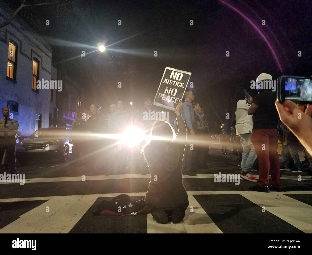A protester holds up a "No Justice No Peace" sign while kneeling in the ...