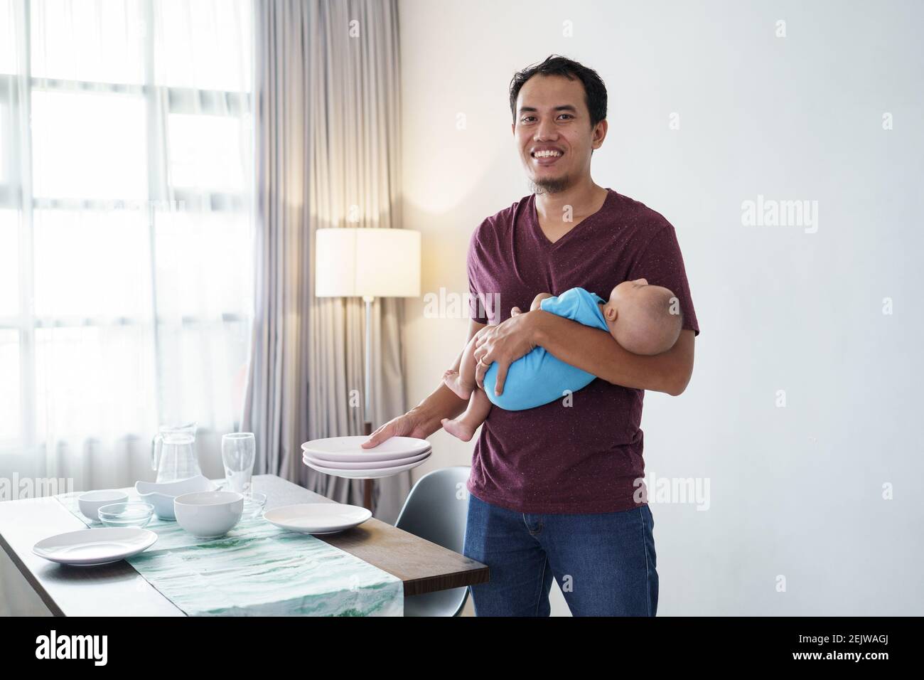 portrait of single father doing chores at home while carrying his baby ...