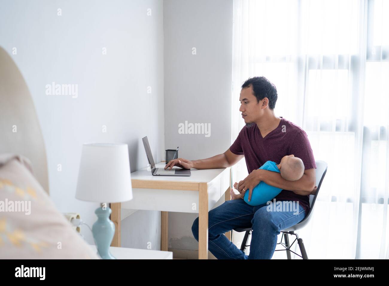 portrait of a busy father working from home while holding his infant ...