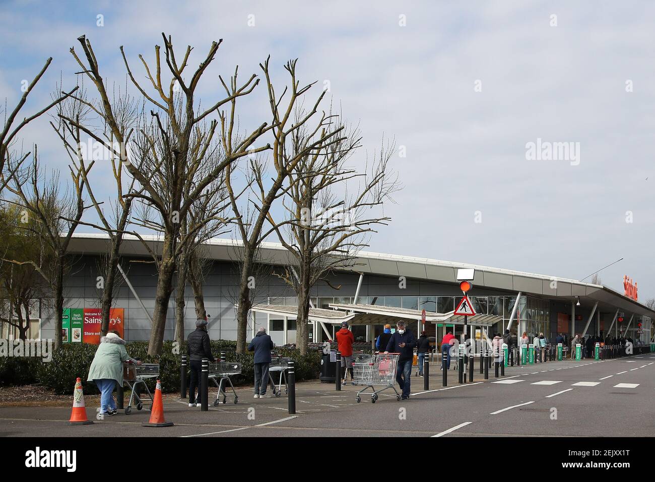 Shoppers queue for their grocery shopping outside Sainsburys in Beckton ...