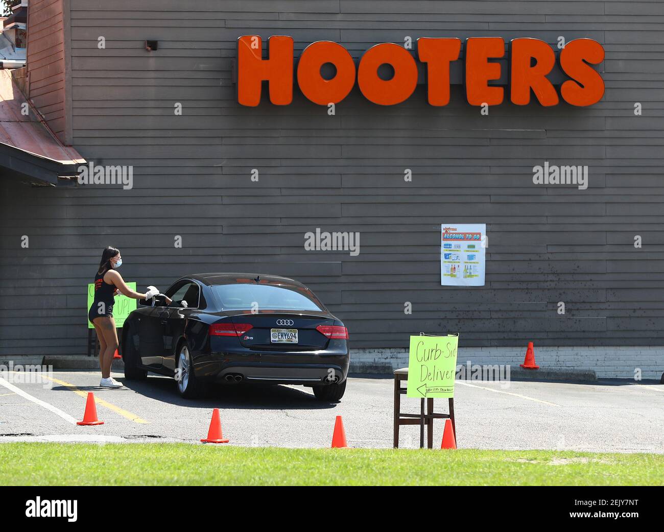 A Hooters girl wearing a mask waits on the one car in the parking lot ...