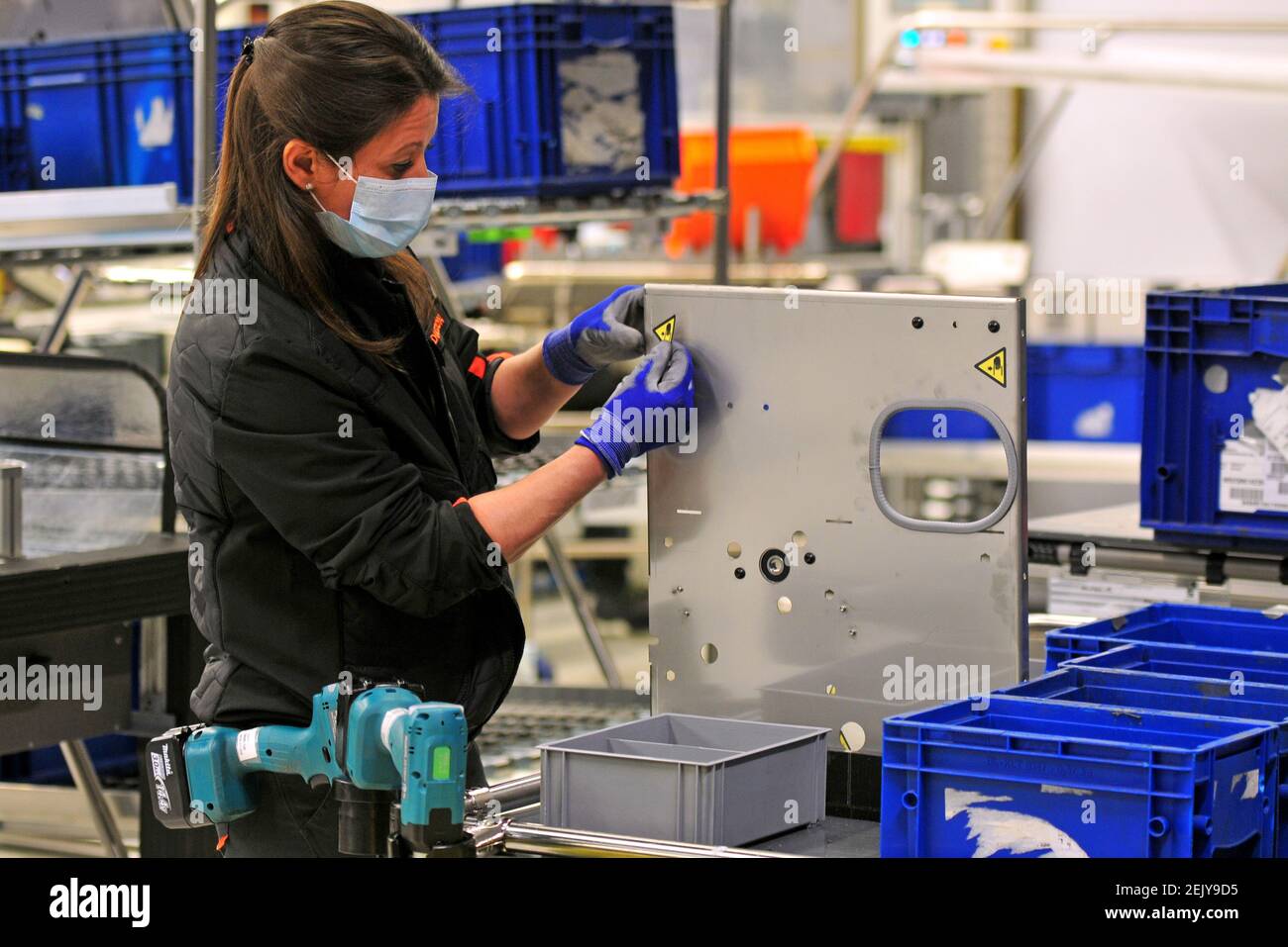 A female assembly operator protected with a surgical mask and gloves ...