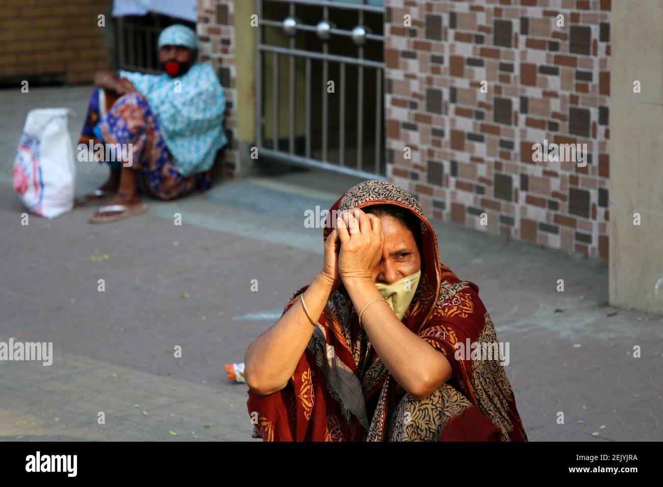 A homeless woman wearing a protective mask awaits for relief on an ...