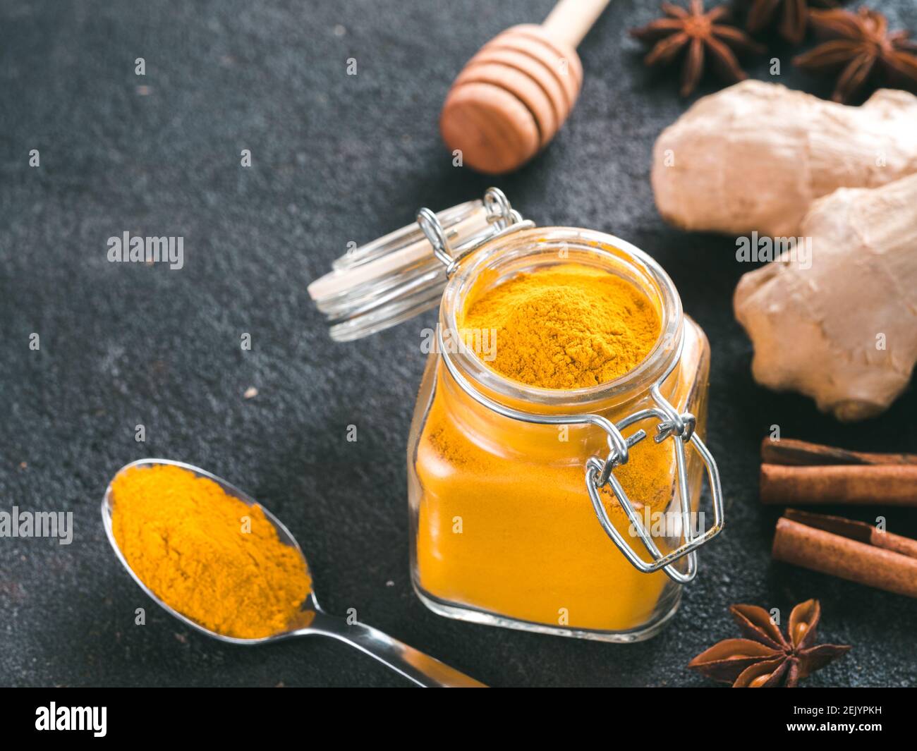Dried turmeric powder in glass jar and spoon on black cement background ...