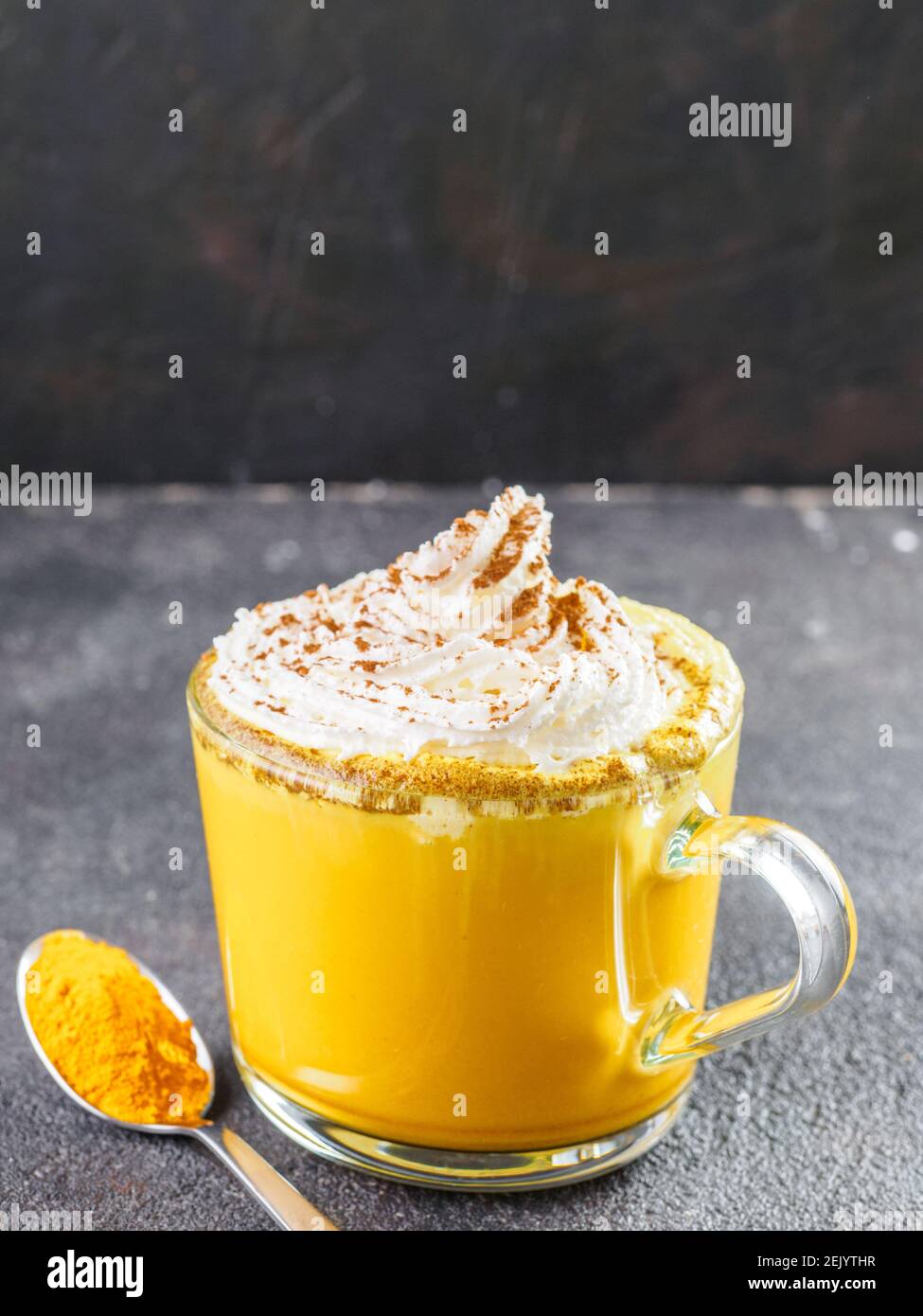 Healthy drink golden turmeric latte with whipped cream in glass cup ...