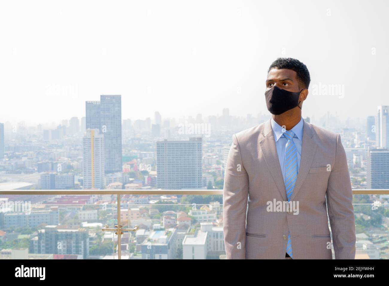 African businessman with face mask for protection at rooftop thinking ...