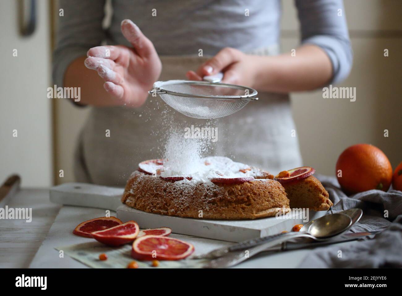 Children's hands sprinkle icing sugar through a sieve on a pie with ...