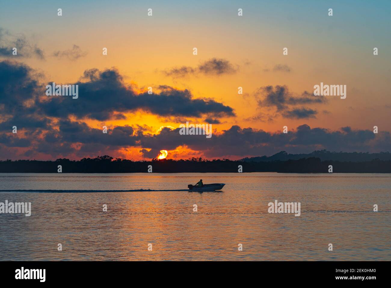 Moody view of a dinghy sailing past the rising sun in a red sky, Miara ...