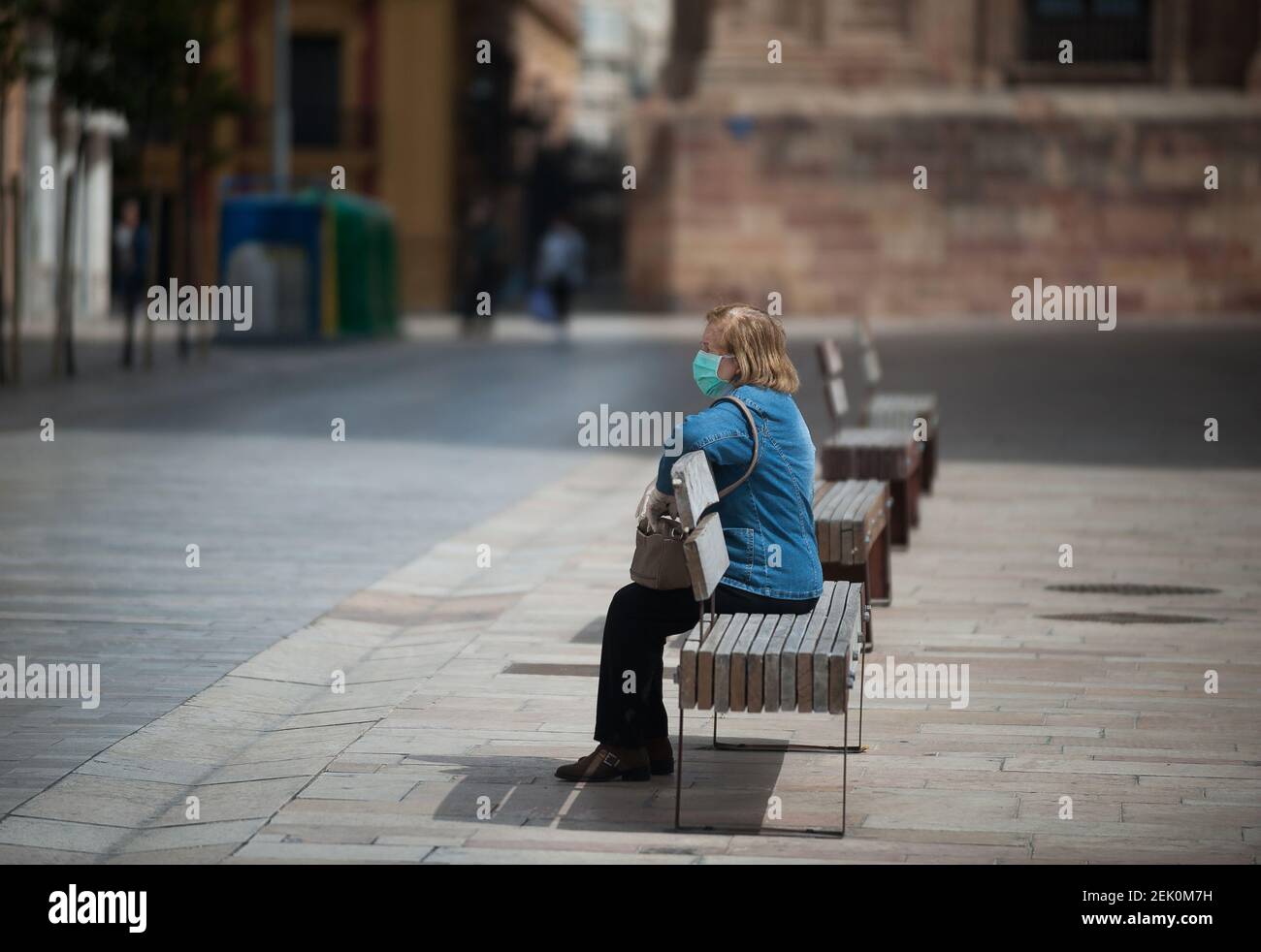 A woman wearing a face mask seating on a bench in a deserted public ...