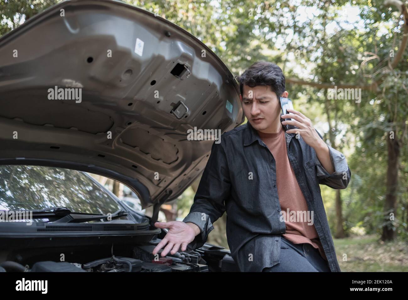 Man use a cellphone call garage in front of the open hood of a broken ...