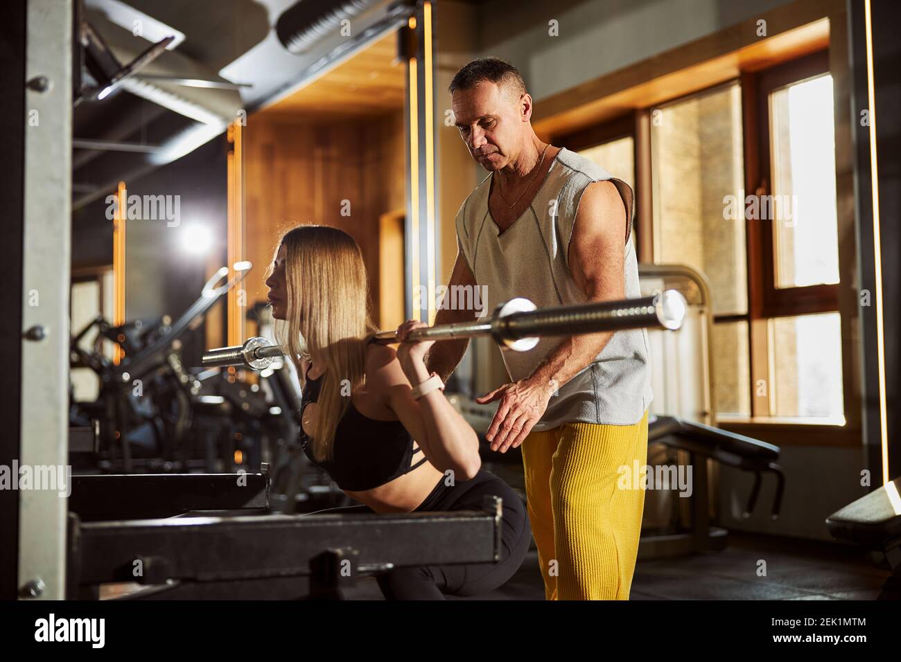 Attentive coach keeping eye on lady lifting weights Stock Photo - Alamy